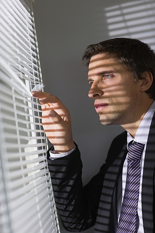 Serious young businessman peeking through blinds in office | 유토이미지 | 상세 ...
