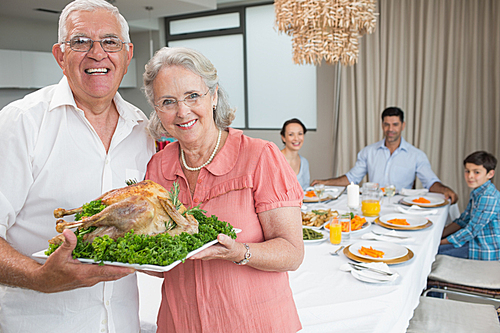 유토이미지 | Grandparents holding chicken roast with family at dining table