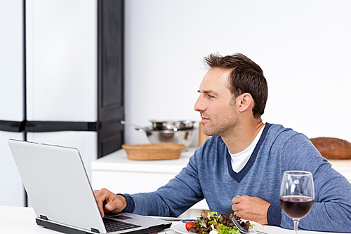 유토이미지 | Focused man looking at his laptop while eating a salad