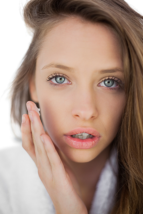 유토이미지 | Pensive brunette in bathrobe rubbing her cheek with cream
