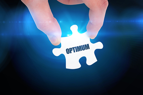 The word optimum and hand holding jigsaw piece against blue background ...