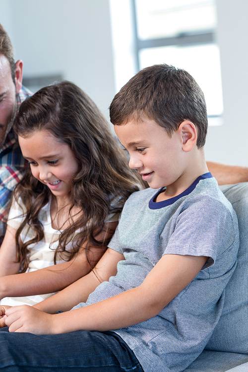 Father and siblings sitting on sofa and using digital tablet in living ...