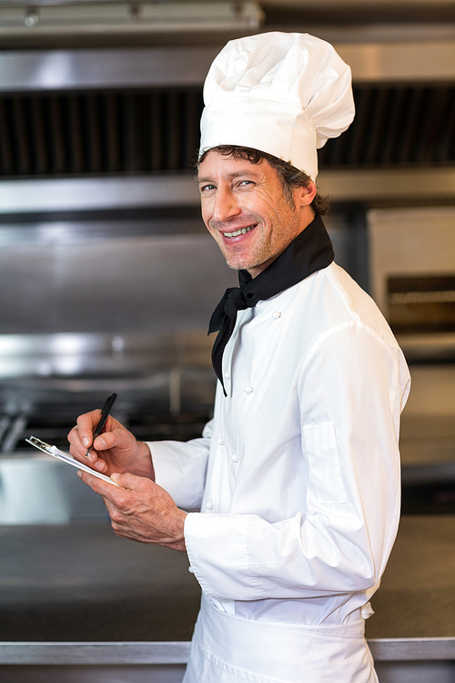 Portrait of smiling happy chef holding clipboard in commercial kitchen ...