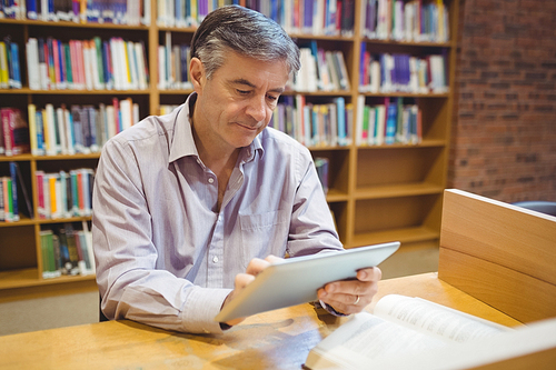 유토이미지 | Professor sitting at desk using digital tablet in college library
