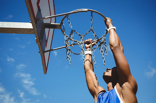 유토이미지 | Close up of teenage boy hanging on basketball hoop against blue sky