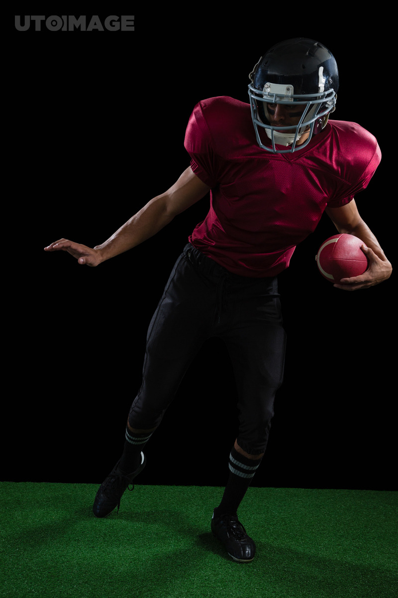 American football player leaning sideways with ball in one of his hand ...