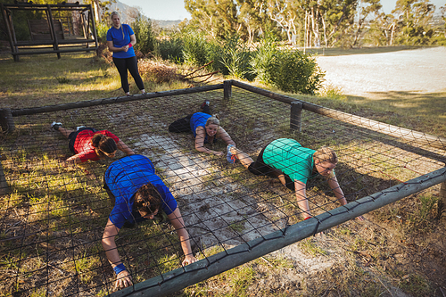 Group of fit women crawling under the net during obstacle course ...