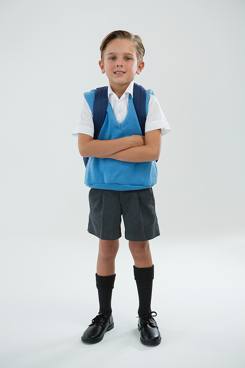 Portrait of cute schoolboy standing with arms crossed against white ...