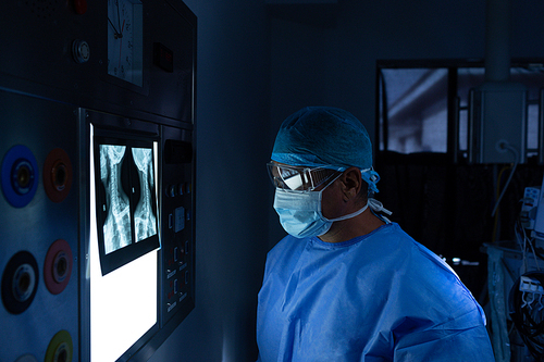Side view of Caucasian male surgeon reading x ray in operating room at ...