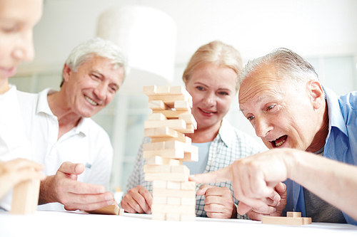 Group of old friends building structure from wooden blocks on table ...