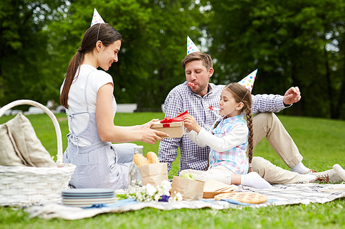 Young parents and their little daughter having birthday picnic in park ...