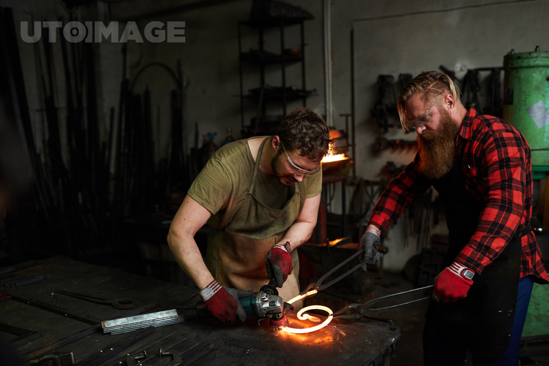 Two professional blacksmiths in workwear standing by anvil and ...