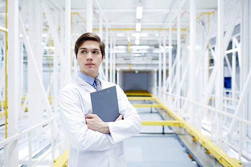 Serious young mining farm worker in whitecoat holding clipboard with ...