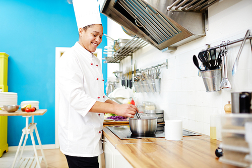 Happy young chef mixing ingredients of boiling food in steel pan in the ...