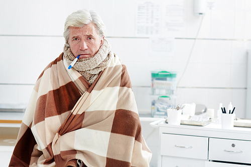 Portrait of senior patient covered in plaid and holding thermometer in ...