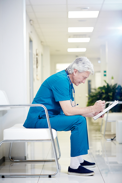 유토이미지 | Male nurse making notes in document while sitting in the corridor