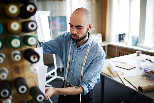 Busy young tailor looking through samples while choosing fabric for new ...