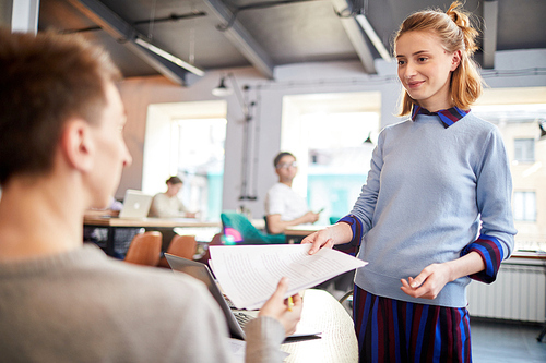 Young businesswoman in casualwear giving papers back to colleague after ...