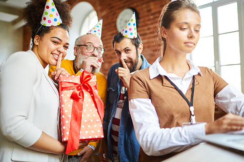Three colleagues making shh gesture while preparing birthday surprise ...