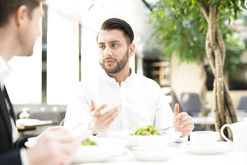 Young manager and his colleague sitting by served table in cafe, having ...