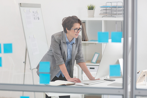 유토이미지 | Woman in formalwear leaning over her desk and looking at ...