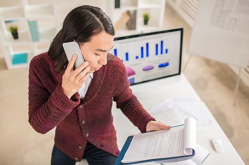 High angle view of concentrated Asian manager in knitted cardigan ...