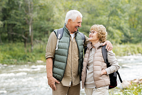 Two cheerful mature backpackers looking at one another in natural ...