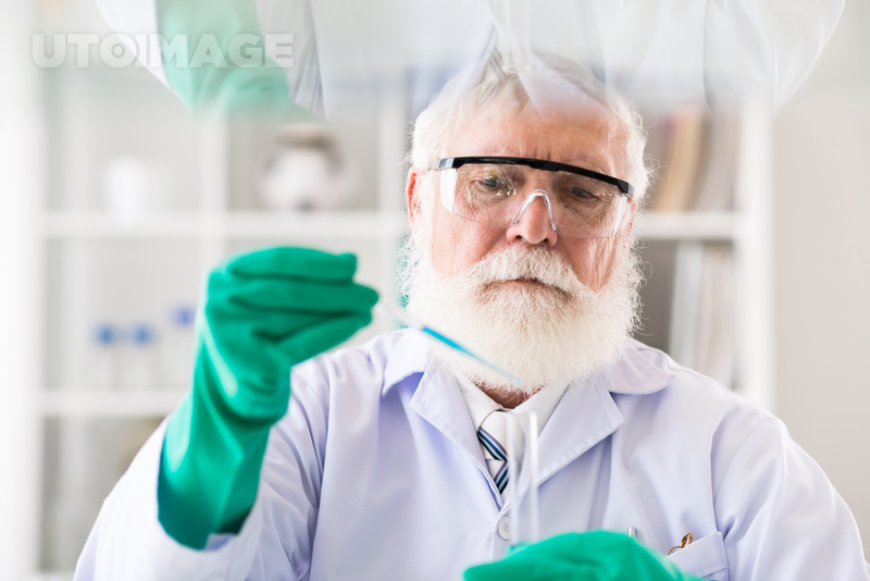 Senior bearded scientist wearing white coat and protective goggles ...