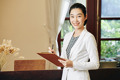 Portrait of lovely spa salon manager taking notes in document on ...