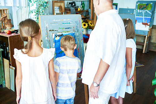 Back view portrait of three children painting on easels during art ...