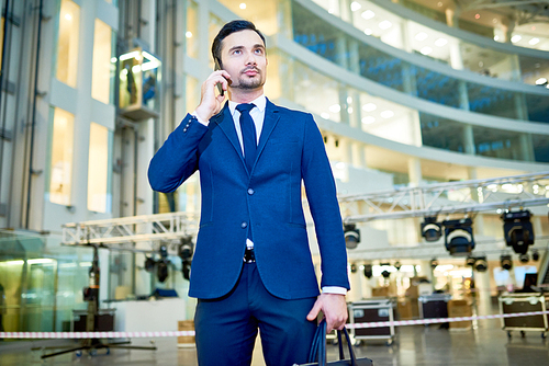Portrait of handsome businessman speaking by phone in lobby of modern ...