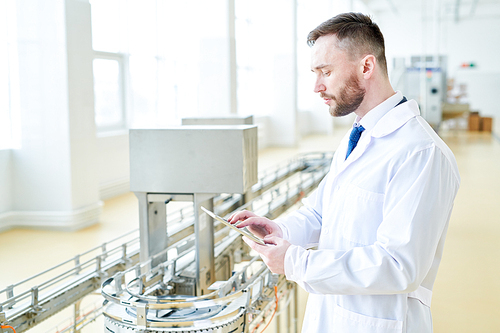 Profile view of confident bearded machine operator wearing white coat ...