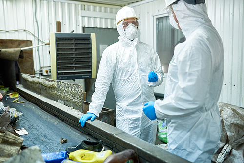 Portrait of two workers wearing biohazard suits communicating standing ...