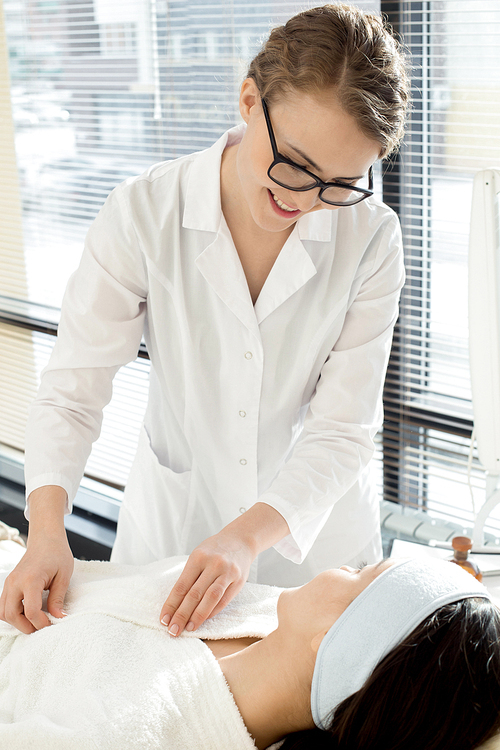 Portrait of smiling young woman preparing client for beauty treatments ...