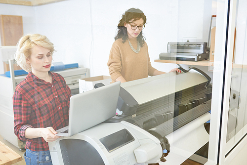 Two lovely women standing in printing office and using laptop and ...