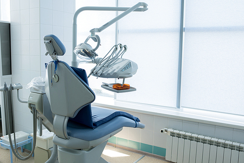 Blue colored seat and working objects of dentist placed in light modern ...