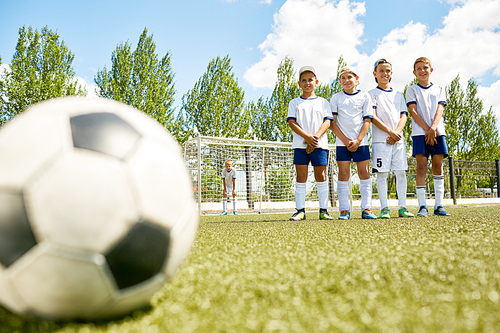 Boys of junior football team standing in row on field with ball in ...