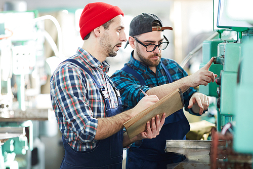 Side view portrait of two new factory workers in training, explaining ...