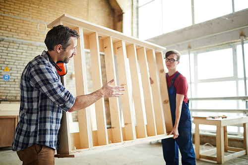 Serious strong workmen carrying wooden bed frame in workshop, they ...