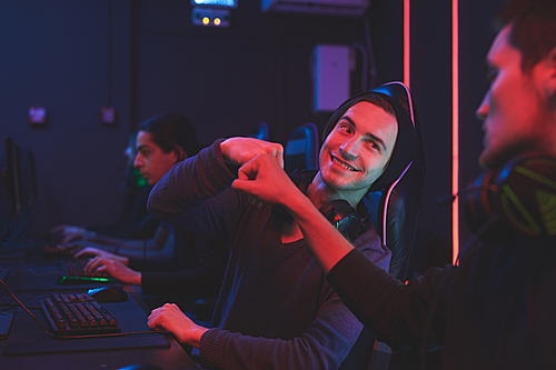 Team of computer gamers sitting at table and making fist bump while ...