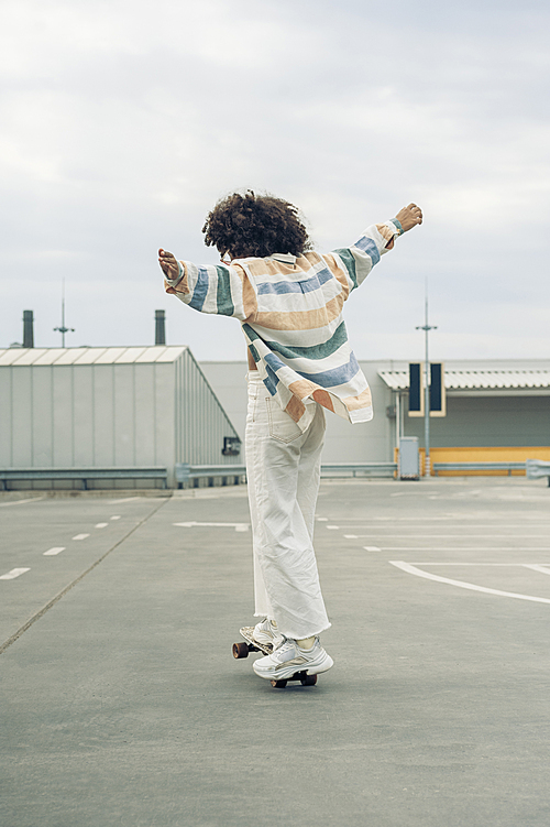 back view of young woman with open arms skateboarding on street | 유토이미지 ...