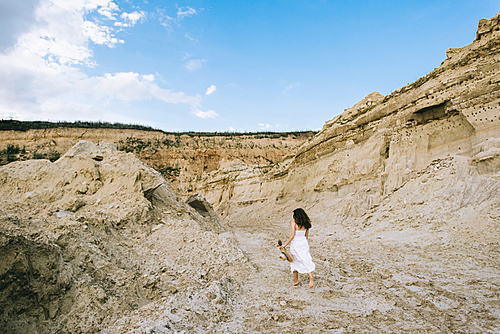 back view of girl in white dress walking in sand canyon with blue sky ...