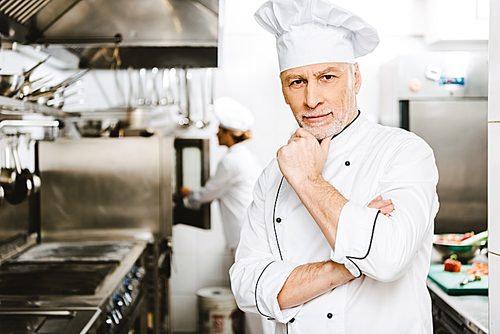 handsome male chef propping chin with hand and in restaurant kitchen ...