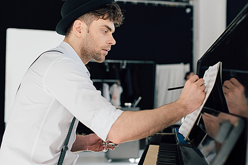 selective focus of handsome composer writing in music book while ...