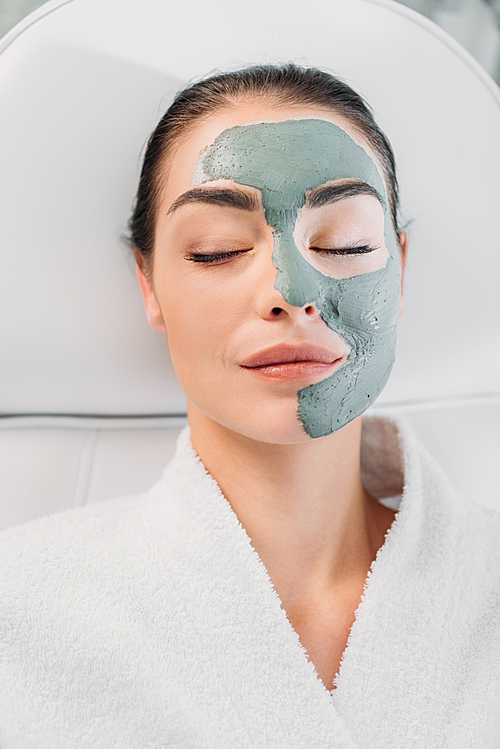 overhead view of beautiful woman with eyes closed and clay mask on face ...