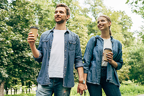 bottom view of happy young couple with paper cups of coffee walking by ...