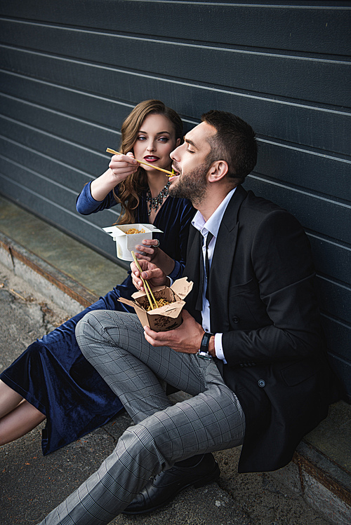 유토이미지 | couple in fashionable clothing eating asian takeaway food on street