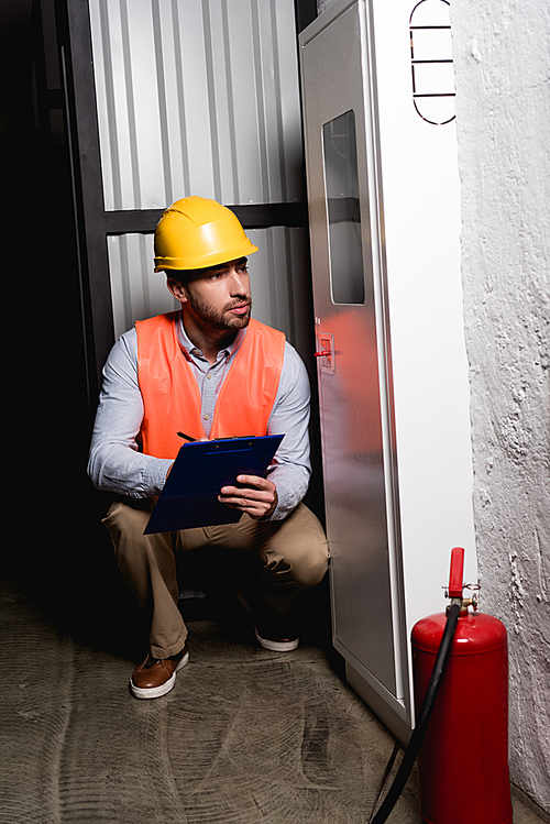 handsome fireman looking at fire panel while sitting and holding ...