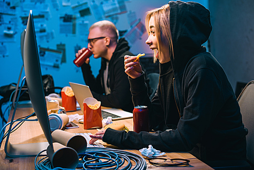 유토이미지 | side view of hackers eating junk food while working on malware