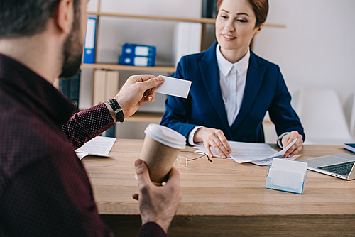 partial view of client with blank card and businesswoman at workplace ...
